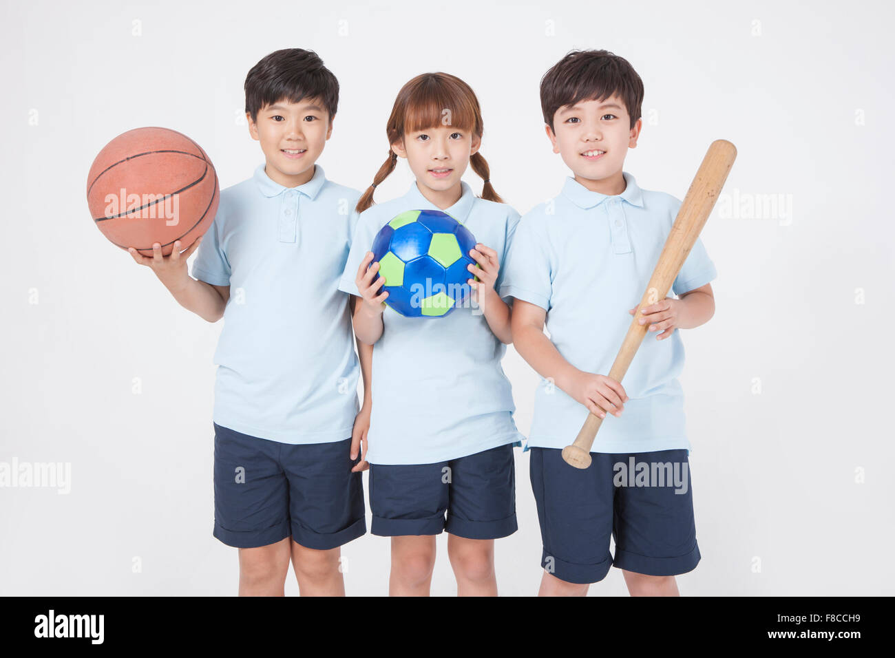 Three elementary students in sports uniforms holding a basketball, a ...