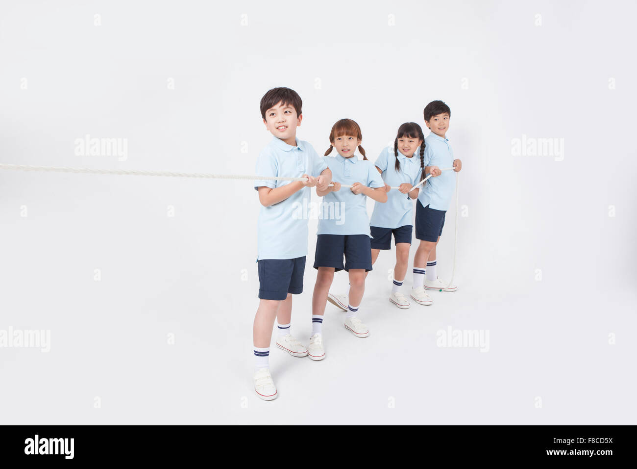 Four elementary school students in sports uniforms holding a rope and ...