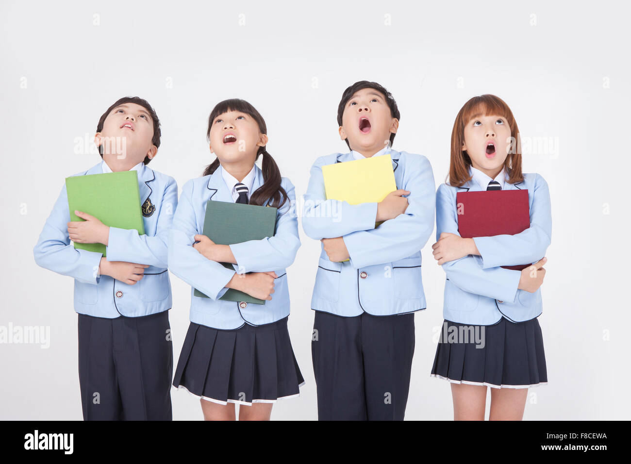 Four elementary school students in school uniforms holding a book each ...