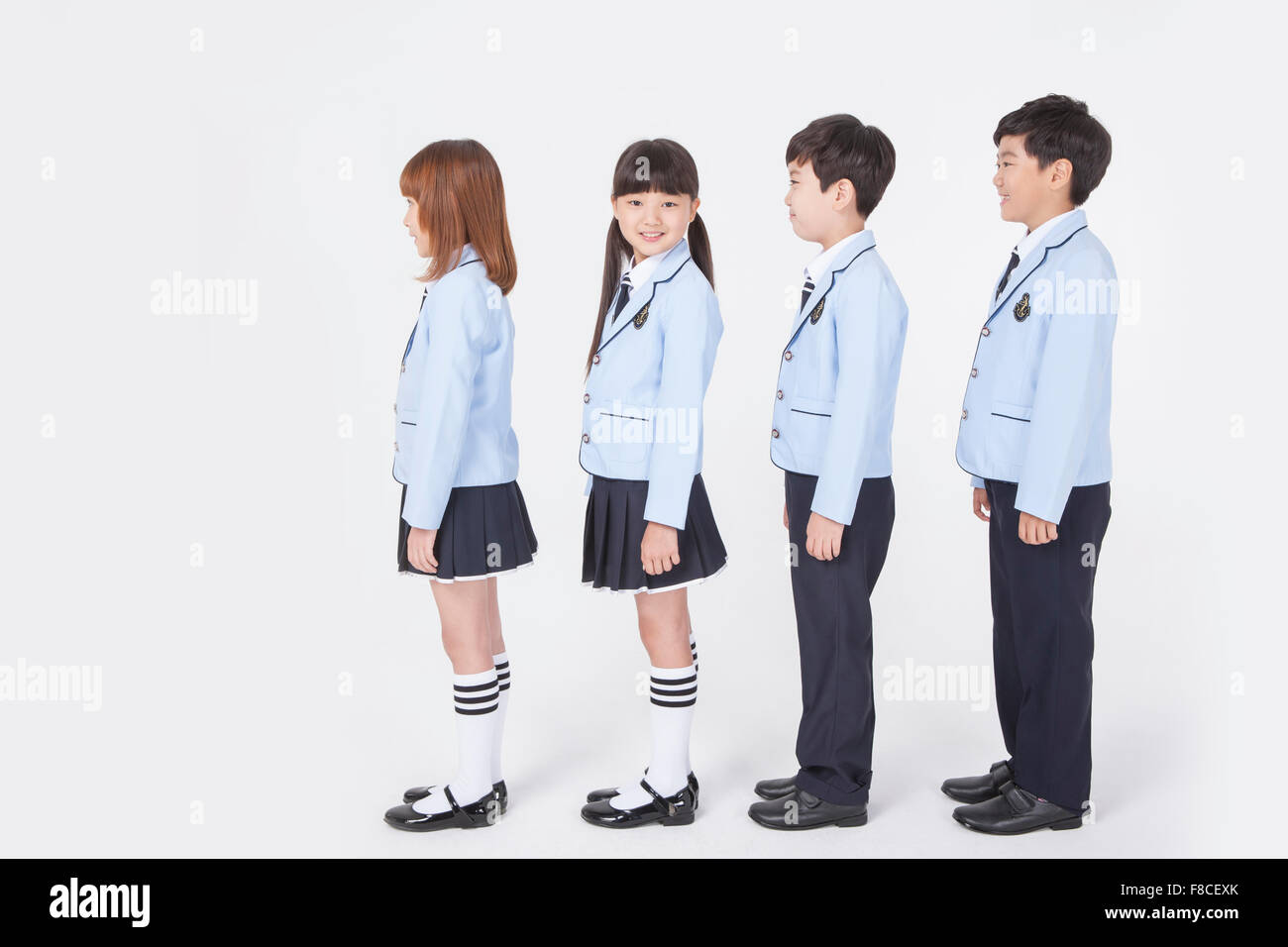 Four elementary school students in school uniforms standing in line and ...