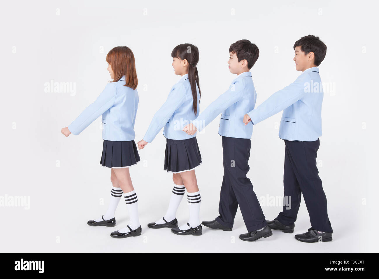 Four elementary school students in school uniforms standing in line and ...