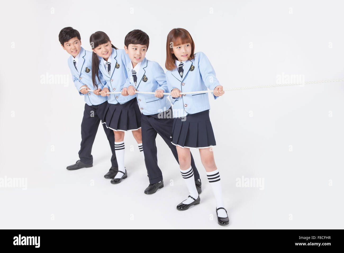 Four elementary school students in school uniforms doing rope-pulling ...