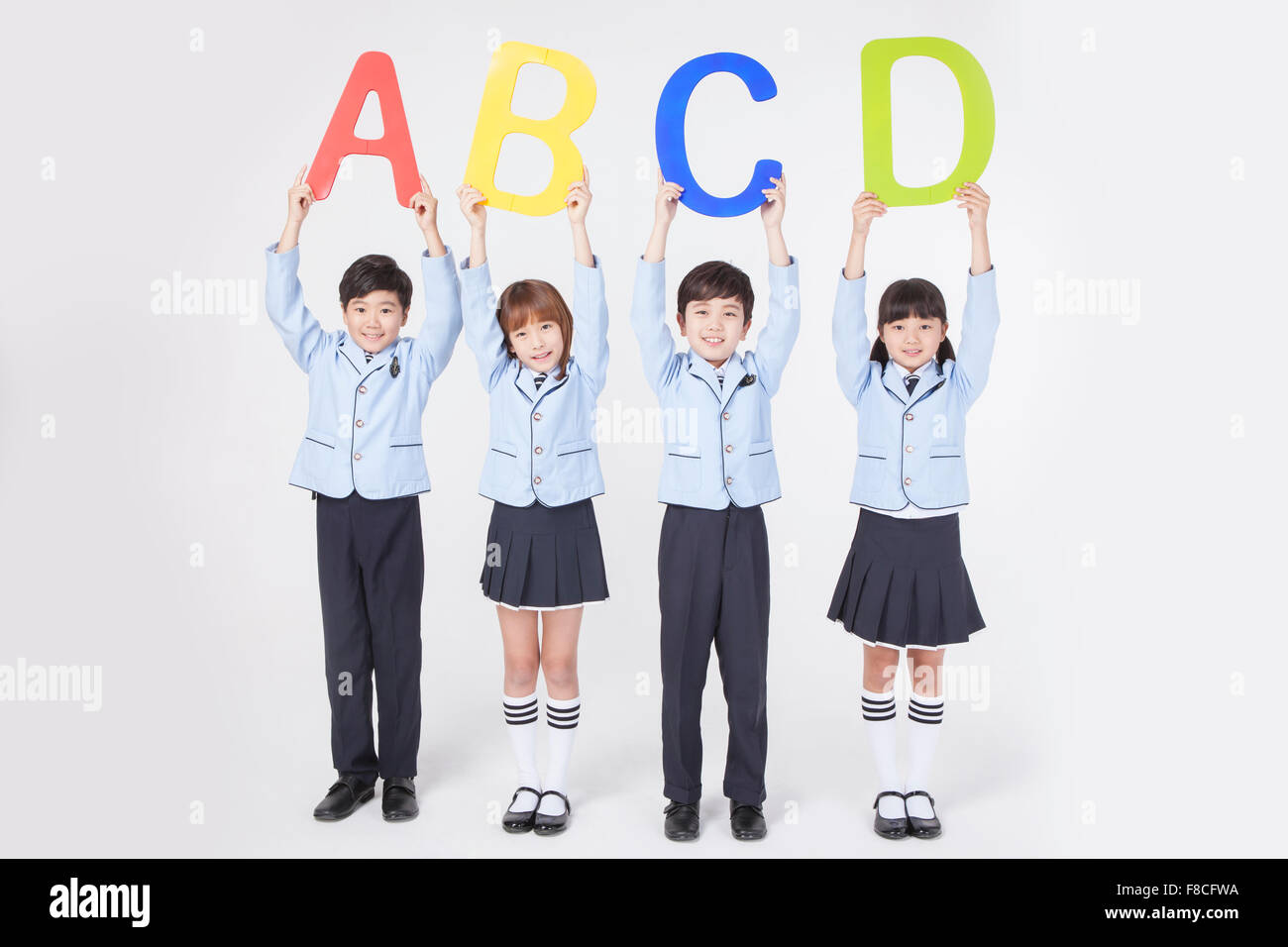 Four elementary school students in school uniforms standing and holding ...