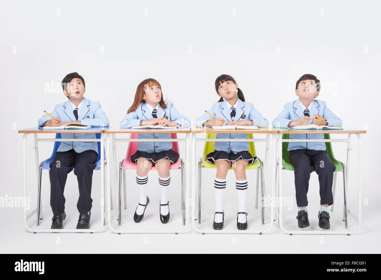 Four elementary school students in school uniforms seated at desk looking up in curiosity Stock ...