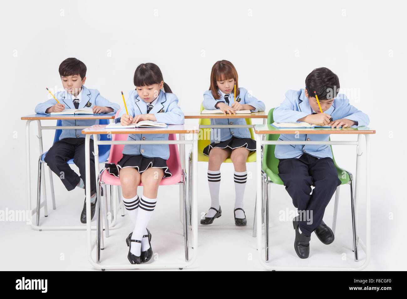 Four elementary school students in school uniforms seated at desk and ...