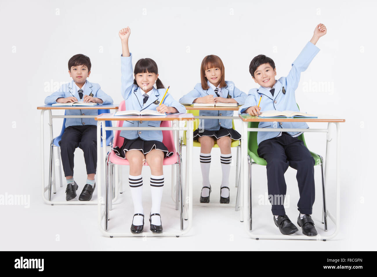 Four elementary school students in school uniforms seated at desk ...