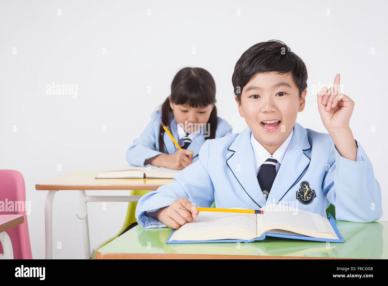 Elementary school boy in school uniforms seated at desk smiling and ...