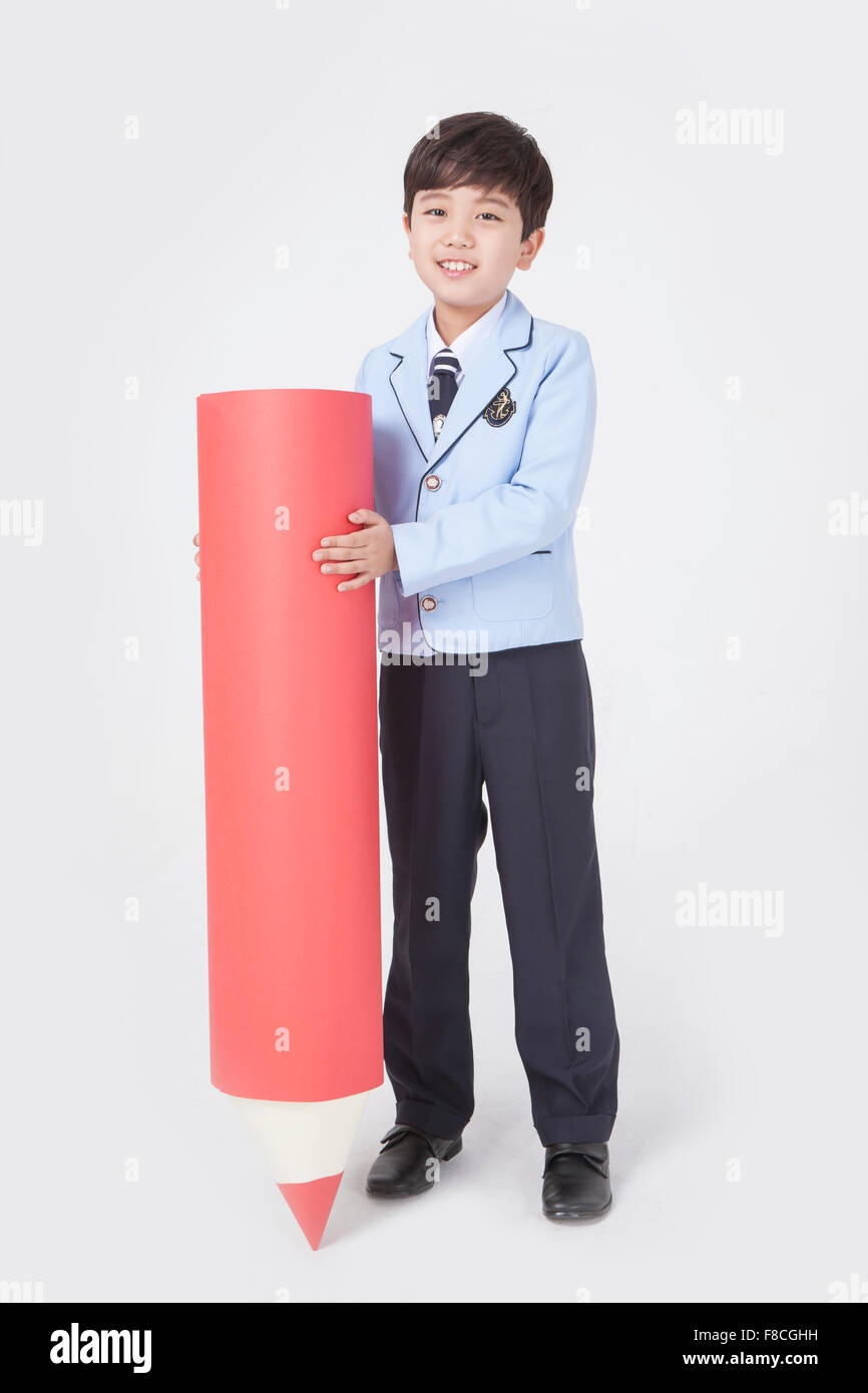 Elementary school boy in school uniforms standing with a big red pencil ...