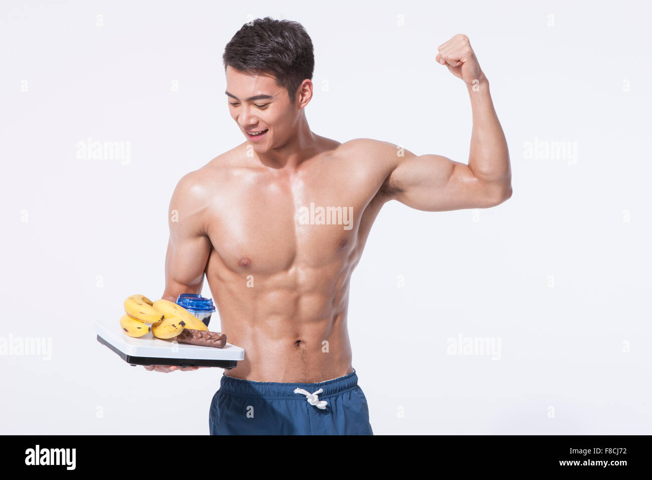 Muscular man showing his biceps and holding a scale with bananas and ...