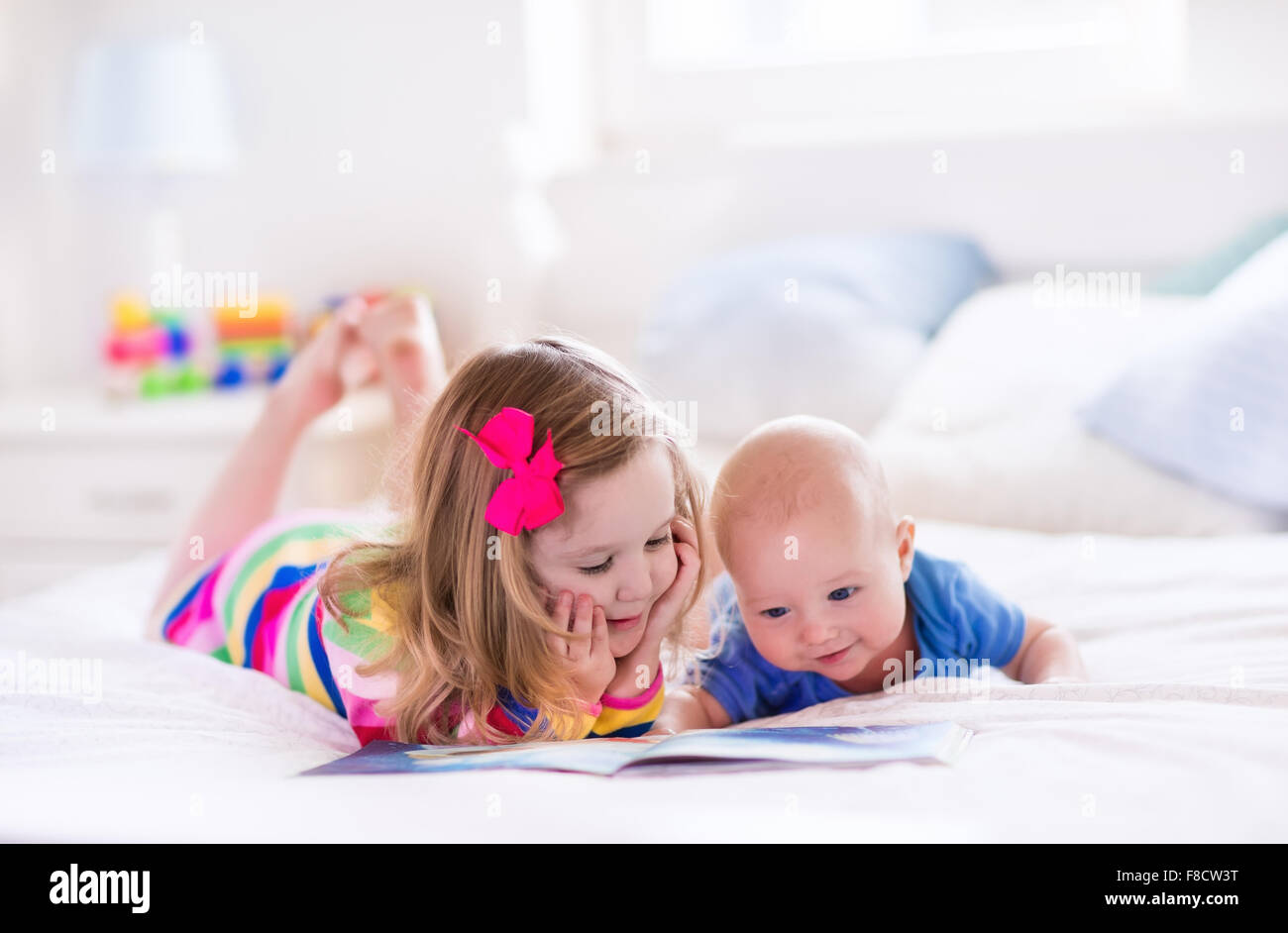 Funny happy toddler girl reading a book and playing with newborn baby ...