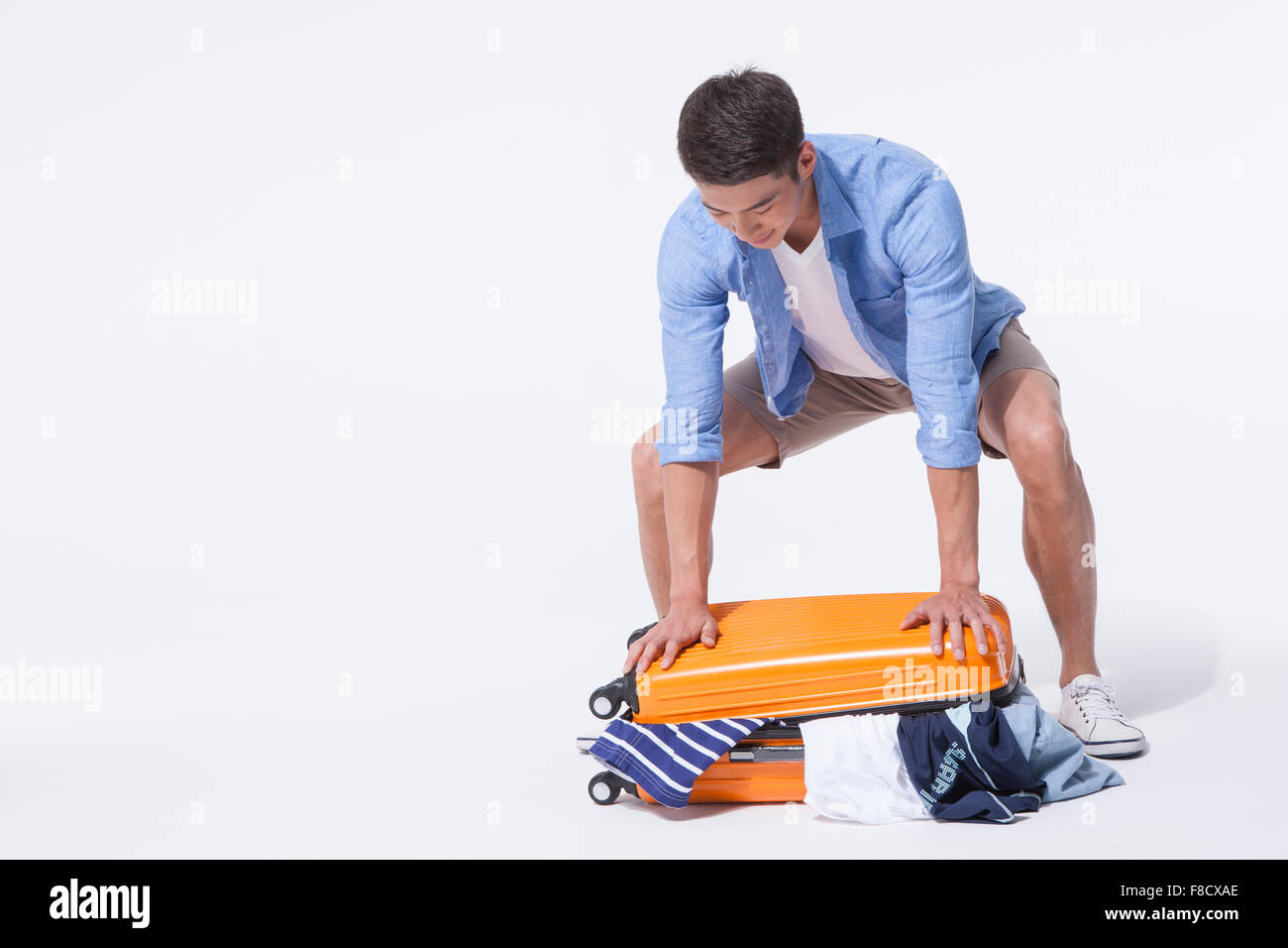 Man in casual outfits packing his clothes in the suitcase looking down ...