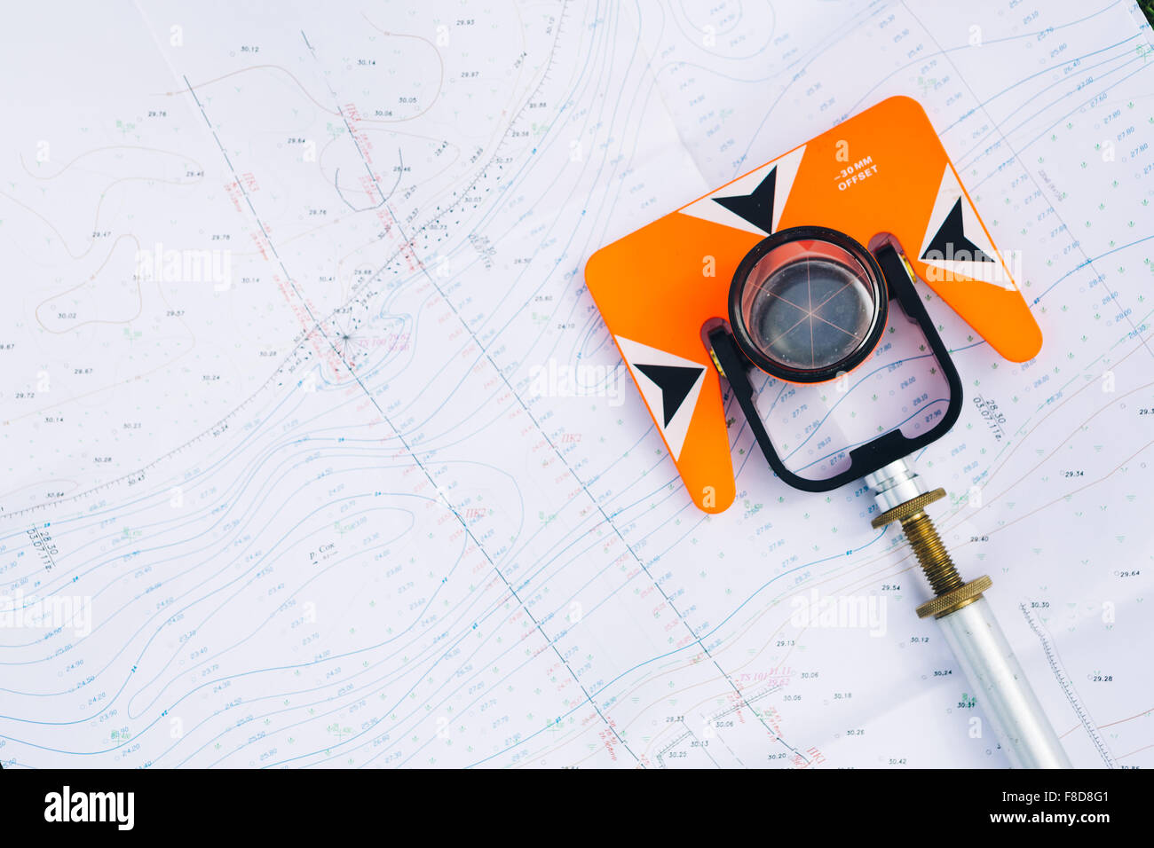 orange theodolite prism lies on a background of geodetic maps of the ...