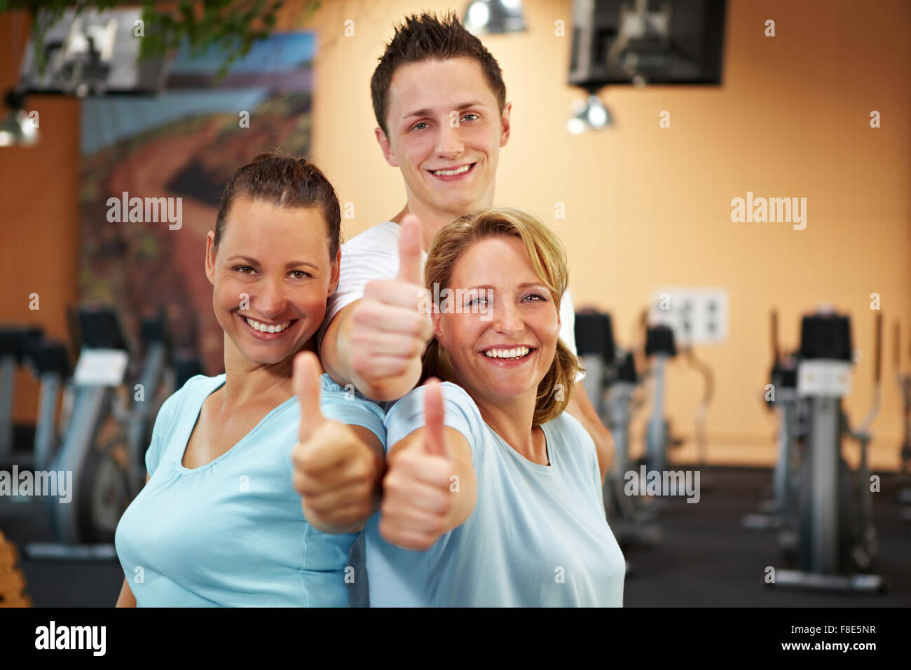 Three happy gym employees holding thumbs up Stock Photo - Alamy