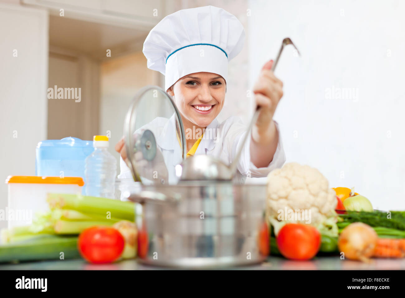 Happy beautiful cook in toque prepares vegetarian lunch at commercial ...