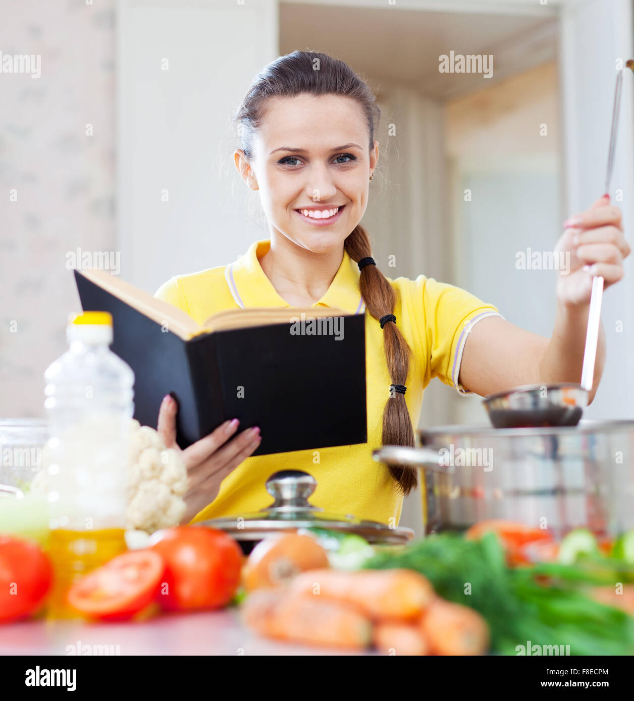 happy woman cooking vegetables with book Stock Photo - Alamy