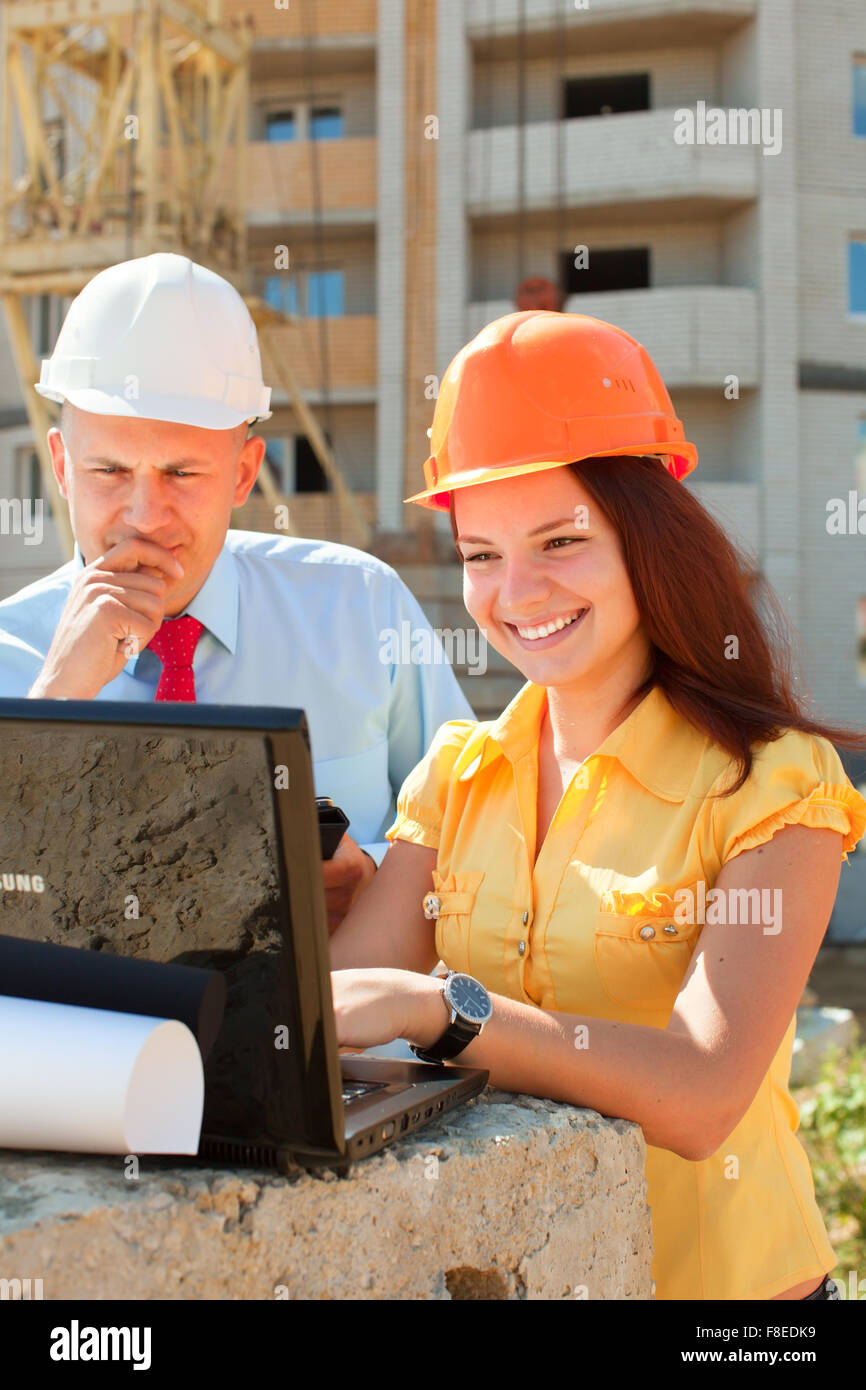 Two architects wearing protective helmet works in front of building ...
