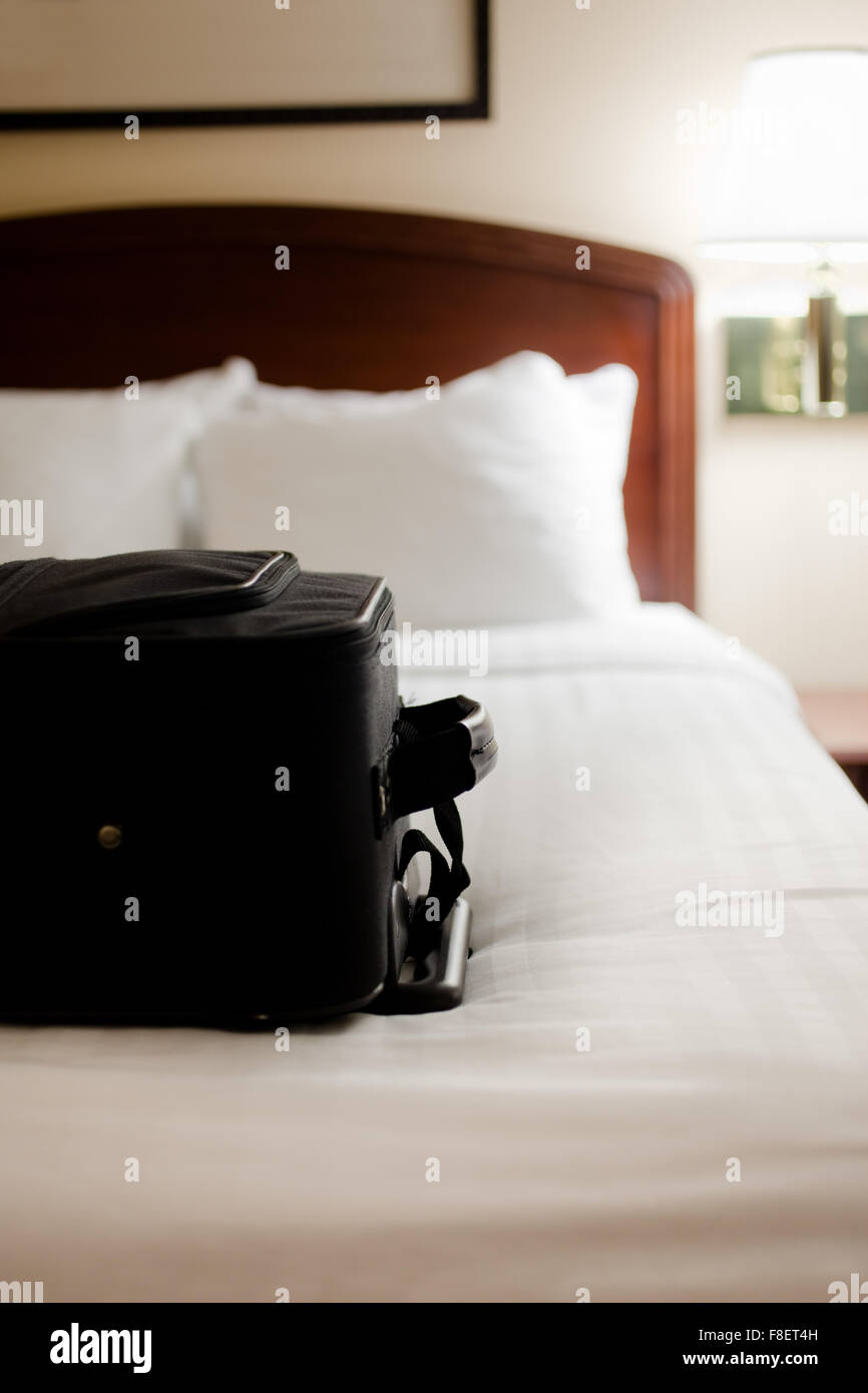 Hotel room bed with a black suitcase and lamp Stock Photo - Alamy