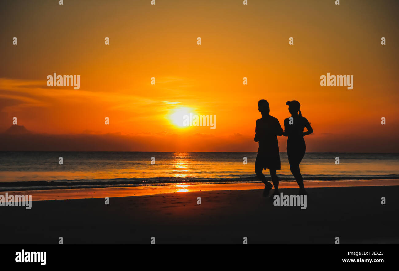 Young couple: man and woman run together on a sunset on lake coast ...
