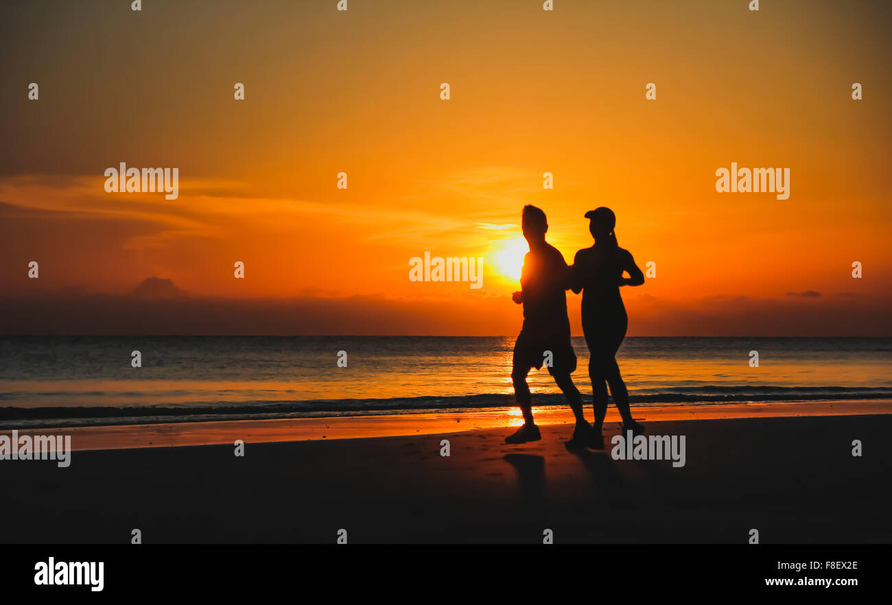 Young couple: man and woman run together on a sunset on lake coast ...