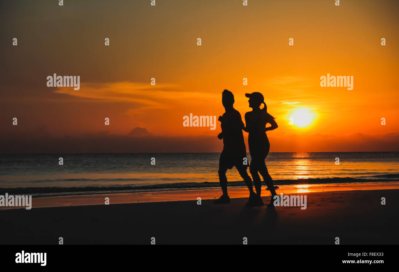 Young couple: man and woman run together on a sunset on lake coast ...