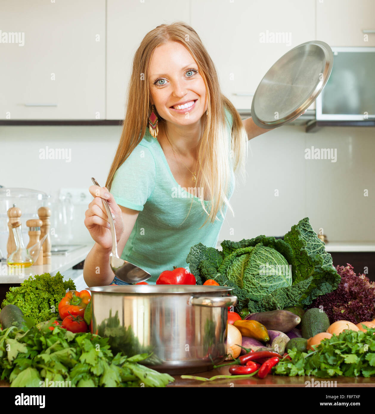 Long-haired woman cooking with ladle from raw vegetables in home ...