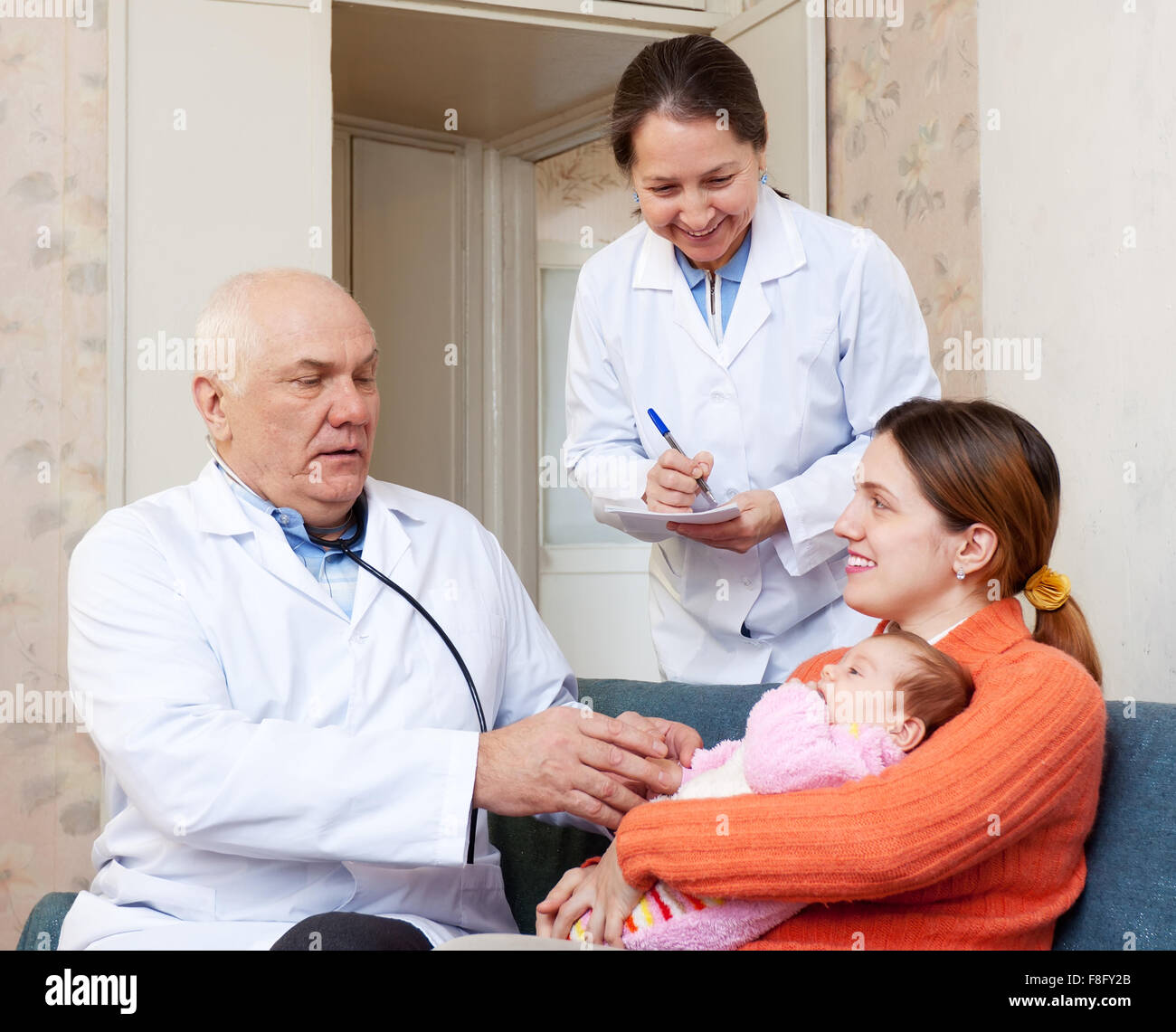 doctors examining little baby in arms of mother. Nurse writes symptoms ...