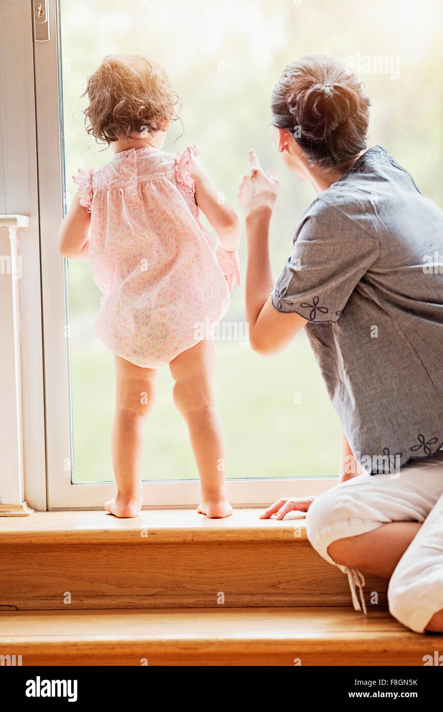 Mother and baby daughter looking out window Stock Photo - Alamy