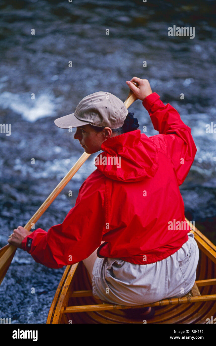 A young woman in a bright red jacket paddles a vintage wooden canoe in ...