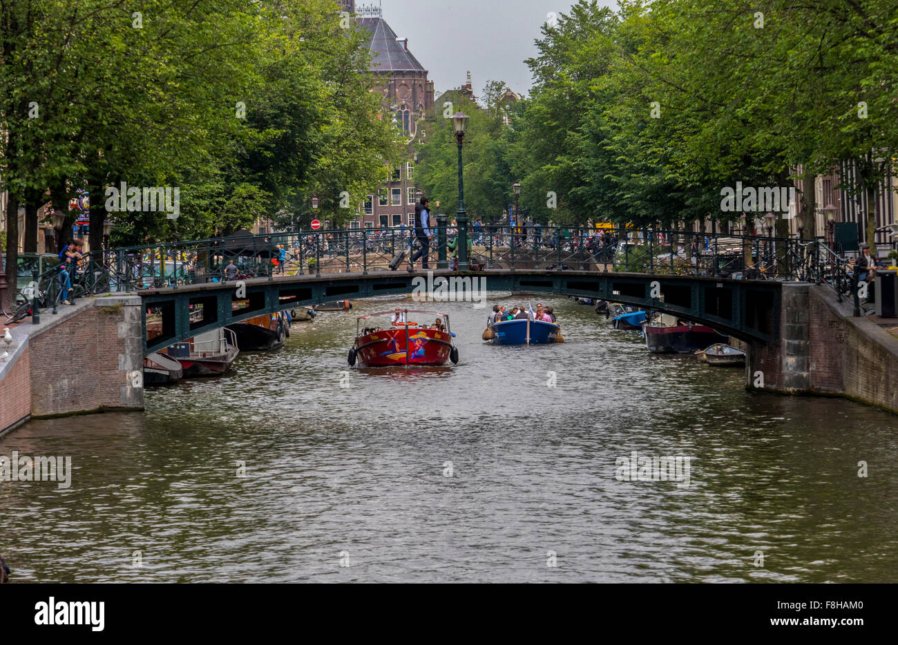 Boats on canal in city of Amsterdam Holland with people crossing bridge ...