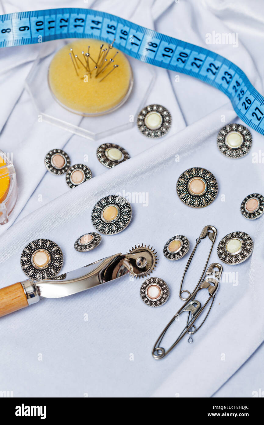 Buttons, pins, measuring tape and needles lying on the silk fabric. The ...