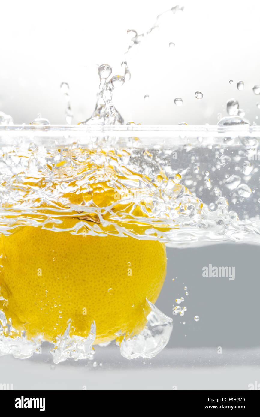 Yellow lemon falling in to water creating splash Stock Photo - Alamy