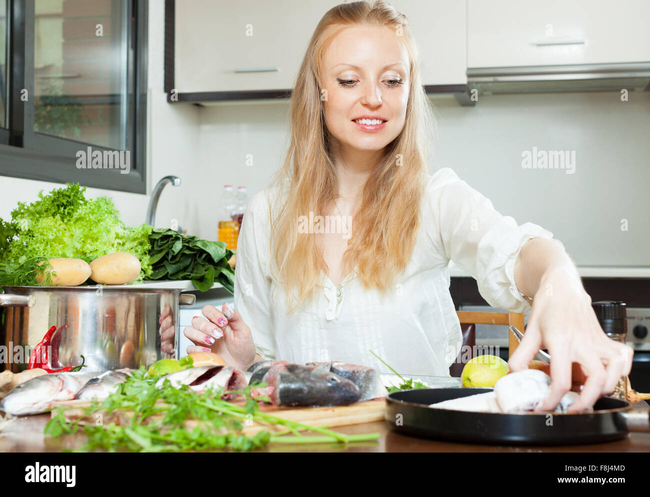 Positive woman cooking fish in flour at kitchen table in home Stock ...