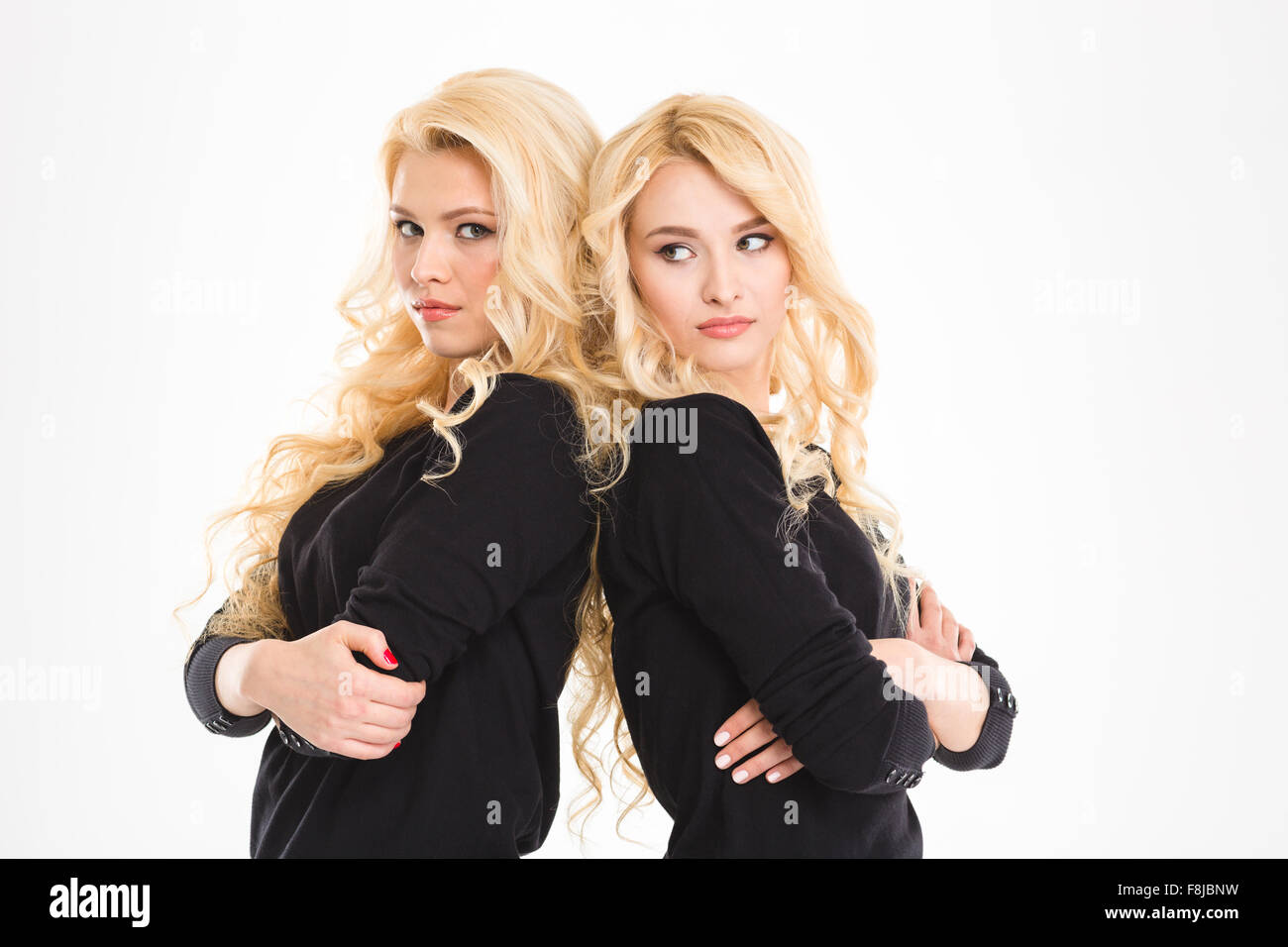Portrait of a young serious sisters twins standing back to back with ...