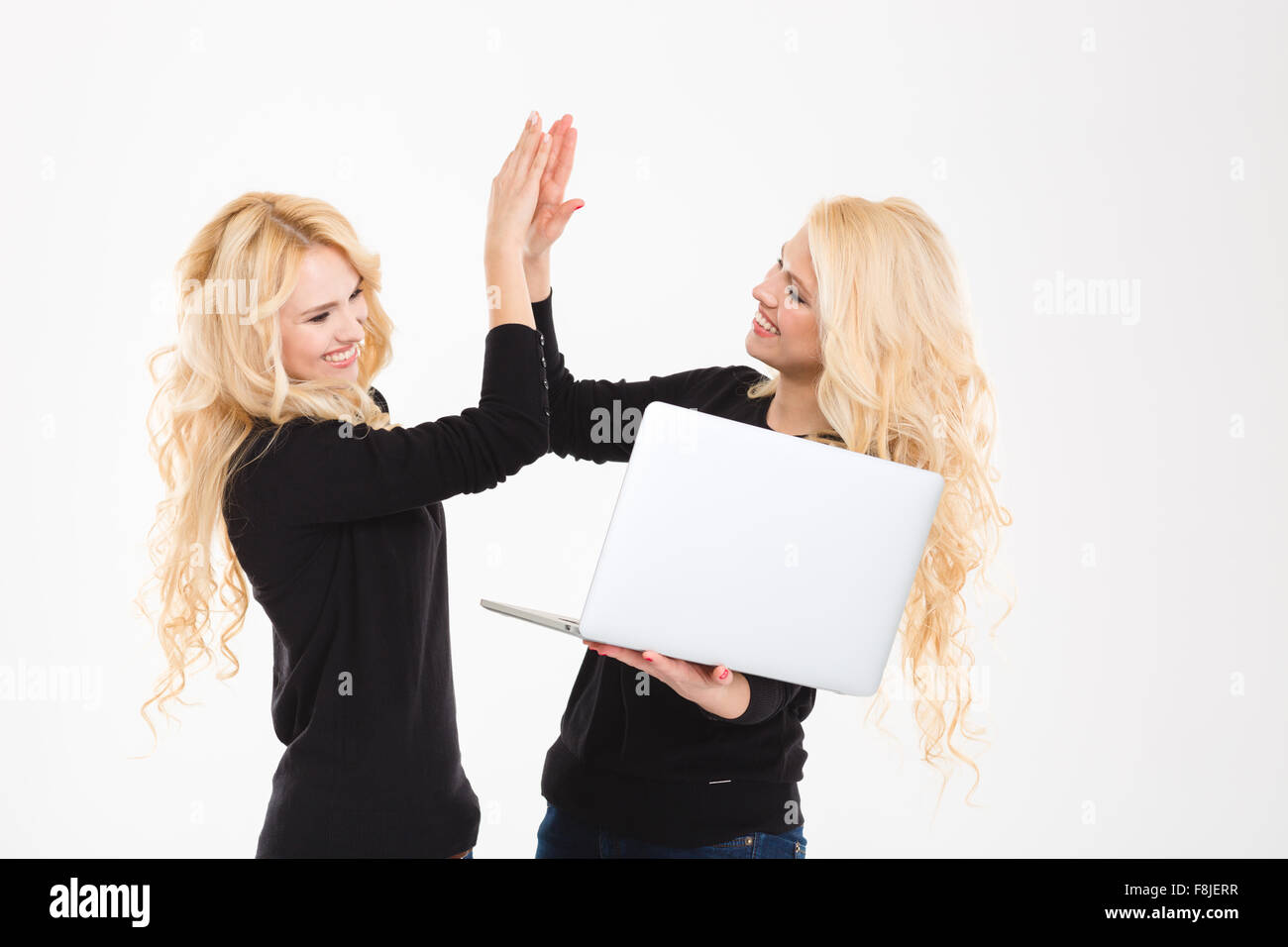 Portrait of a happy sisters twins with laptop computer celebrating ...