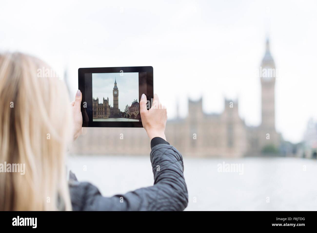 Rear view of young woman photographing Big Ben on digital tablet ...