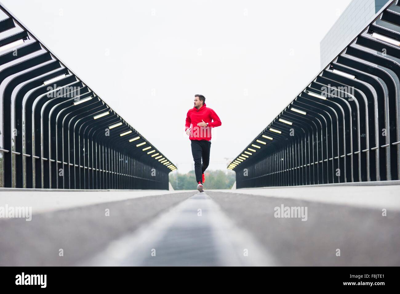 Surface level view of young male runner running over city footbridge ...