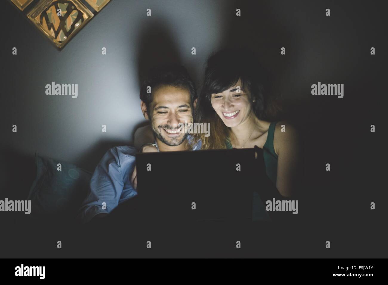 Front view of young couple illuminated by laptop computer screen ...