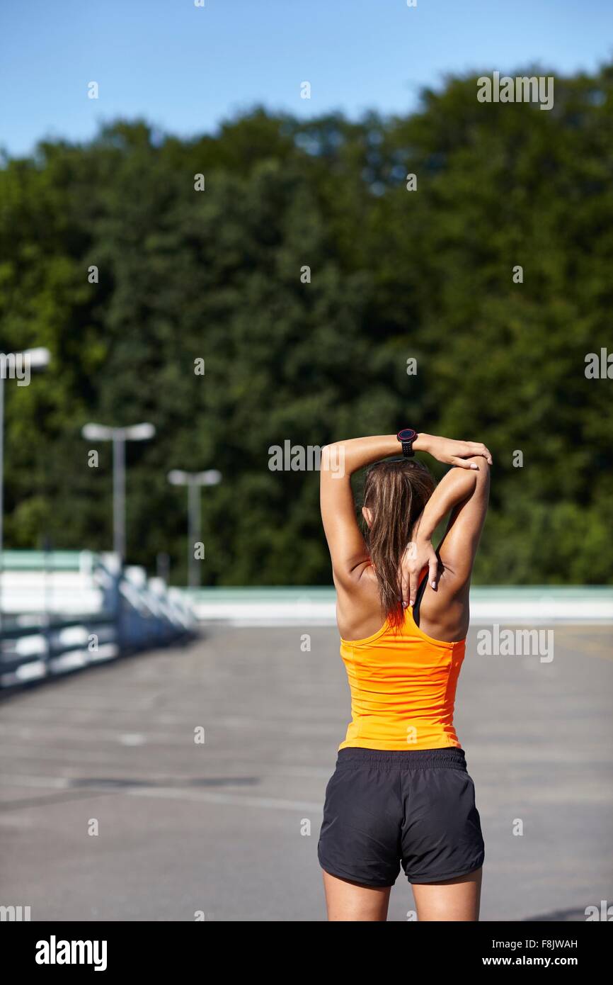 Rear view of young female runner stretching in parking lot Stock Photo ...