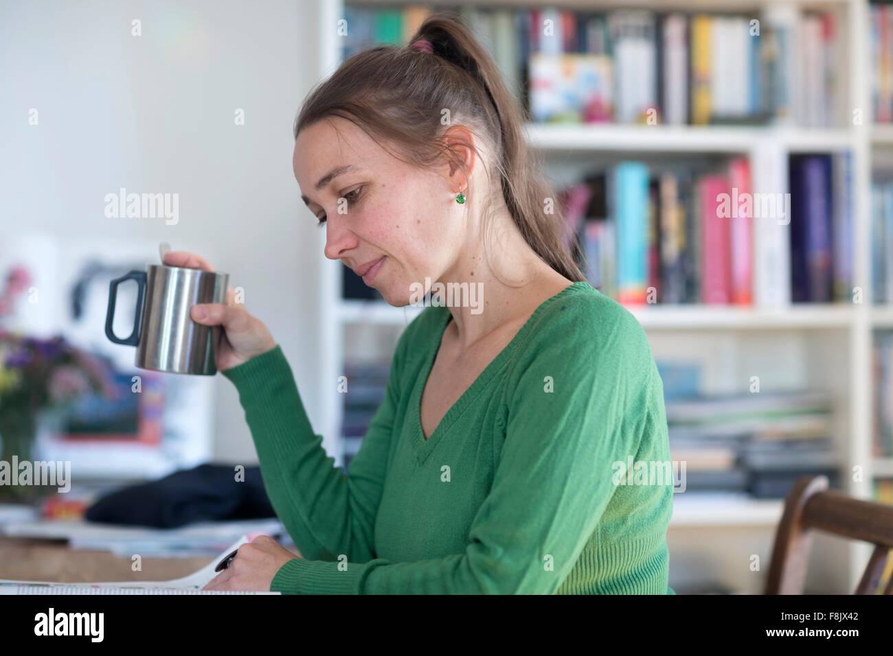Side view of mid adult women sitting at table reading magazine holding ...