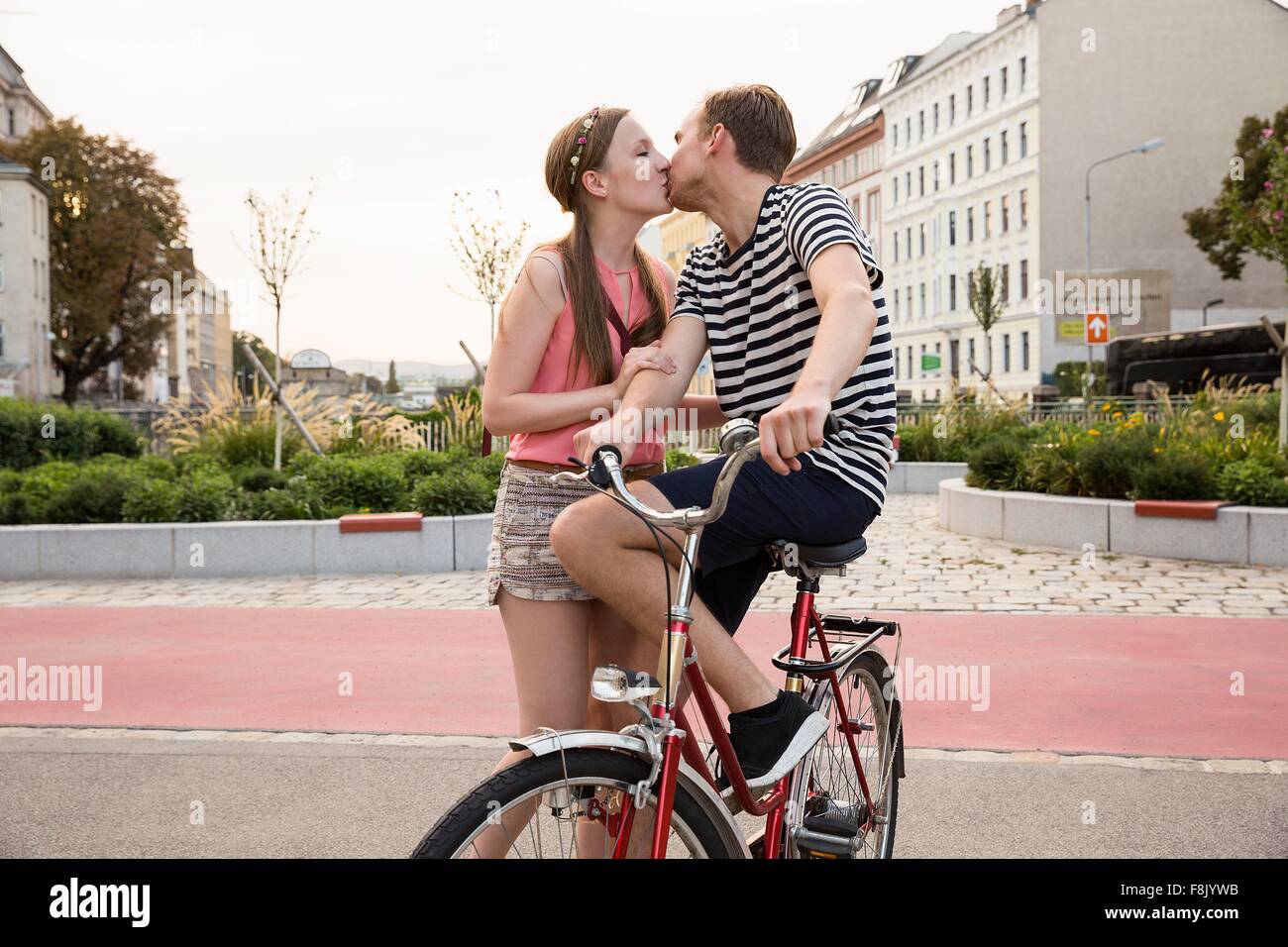 Young man sitting on bicycle kissing young woman Stock Photo - Alamy