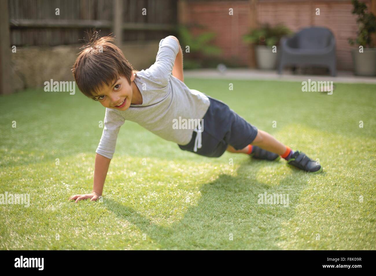 Boy doing one handed push up on grass looking at camera smiling Stock ...