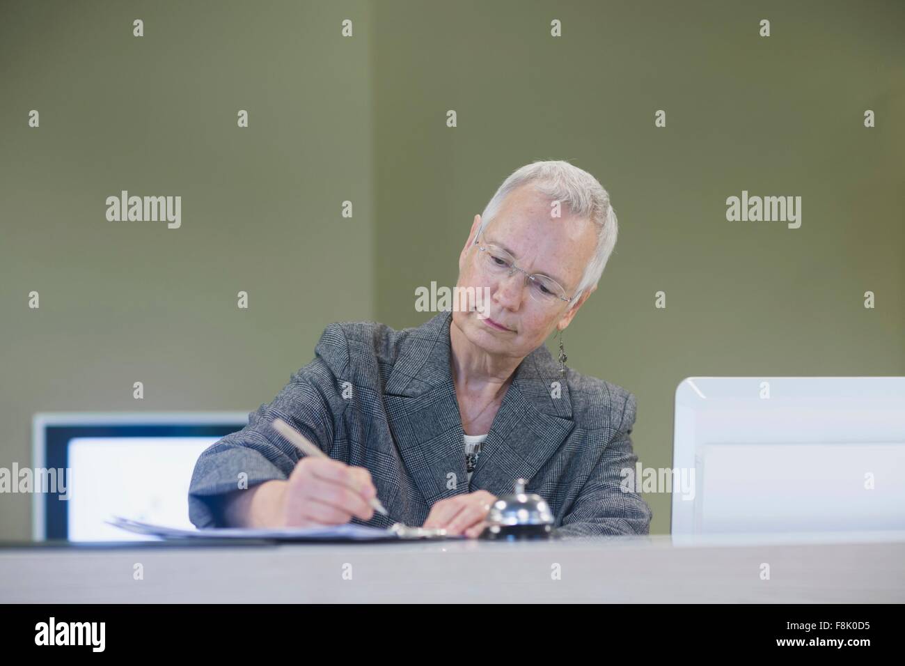 Senior female receptionist writing at hotel reception desk Stock Photo ...