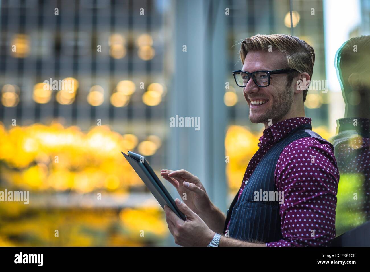 Happy young businessman leaning against park window using digital ...