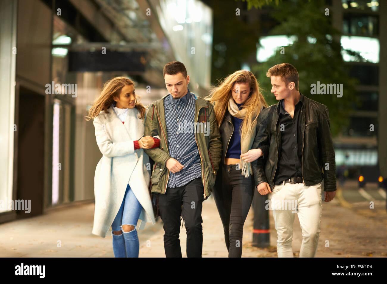 Two young couples strolling arm in arm on street at night, London, UK ...