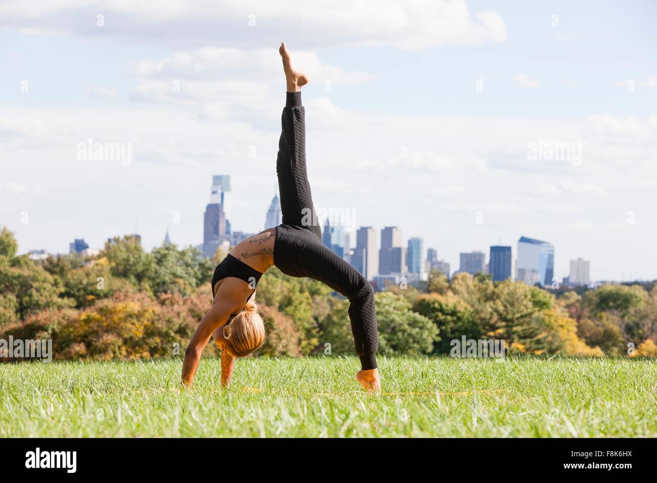 Side view of young woman on grass, bending over backwards, leg raised ...