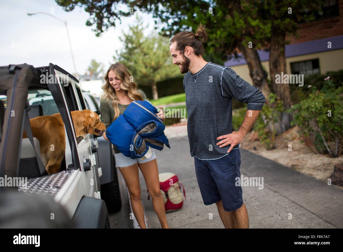 Young couple and dog preparing to load jeep for road trip Stock Photo ...