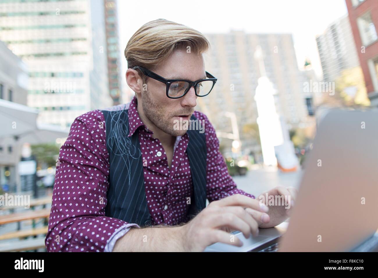 Stressed young businessman typing on laptop at sidewalk cafe, New York ...