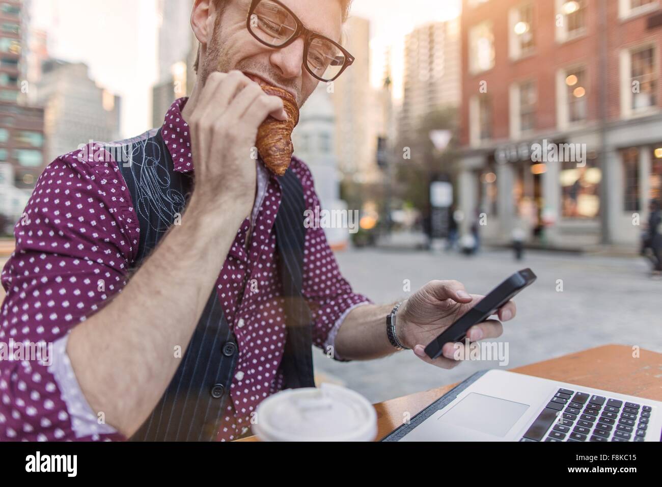 Stressed young businessman reading smartphone whilst eating at sidewalk ...