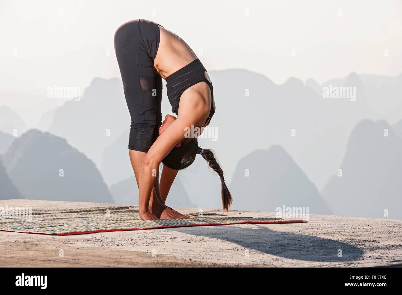 Side view of woman bending over in yoga pose above limestone mountains, Yangshuo, Guangxi Zhuang ...