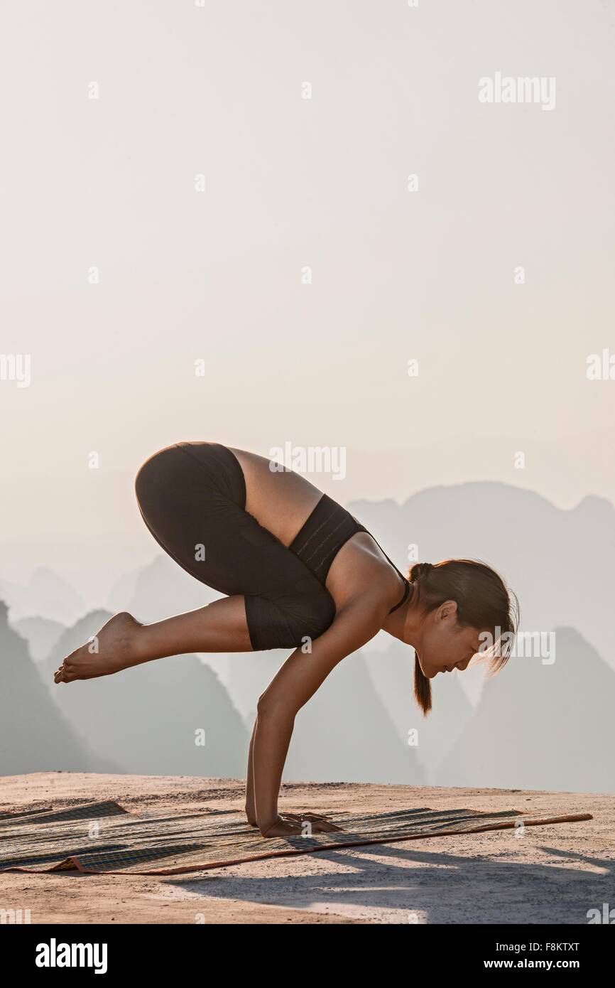 Side view of woman balancing on hands in yoga pose above limestone ...